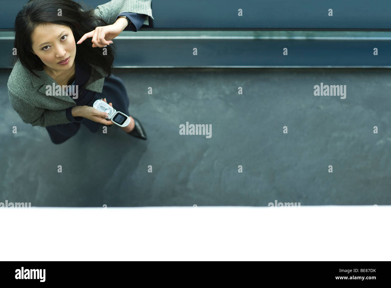 Businesswoman text messaging with cell phone, looking up at camera ...