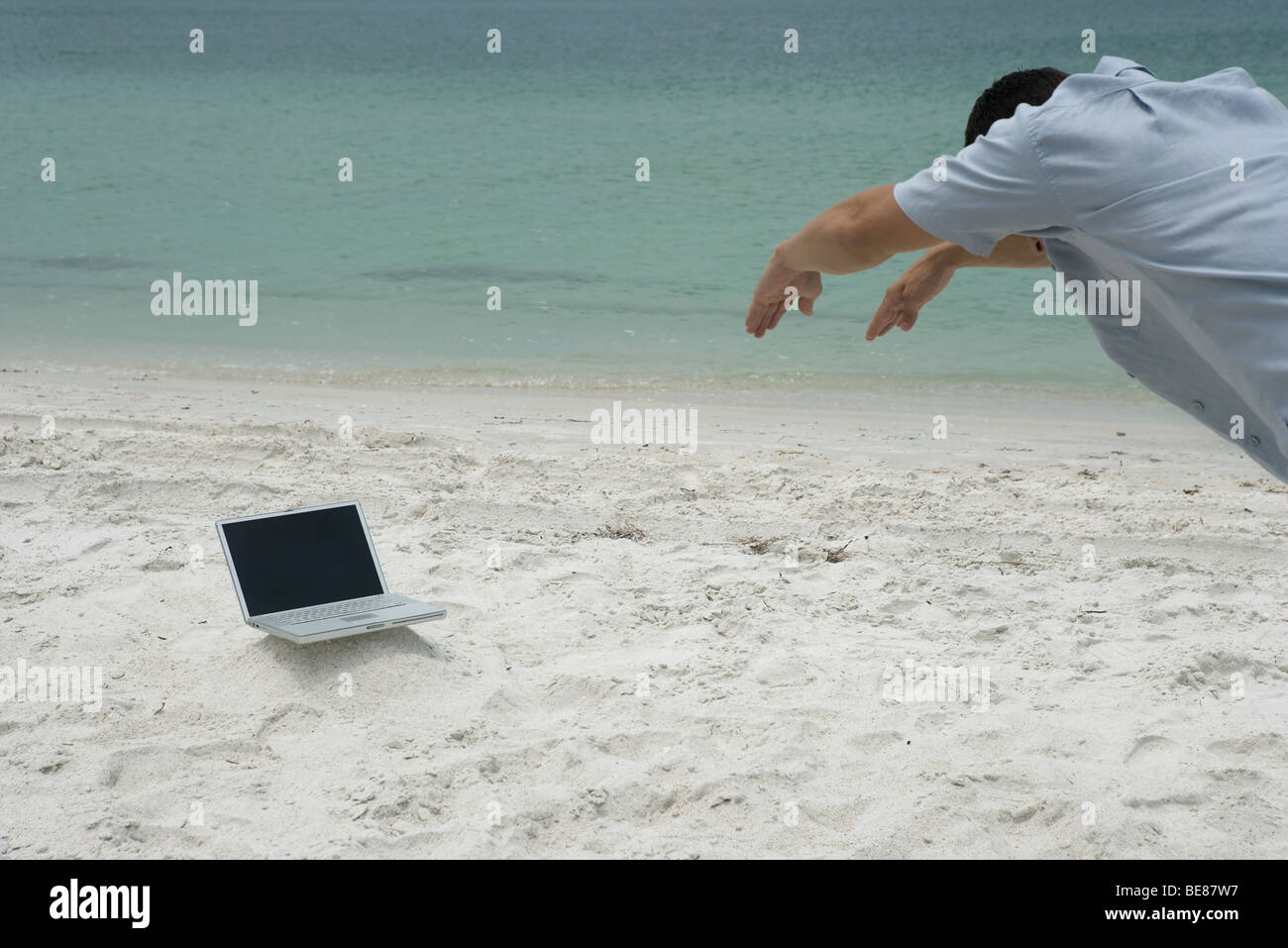 Man at beach, bending over as if diving into laptop computer, cropped ...