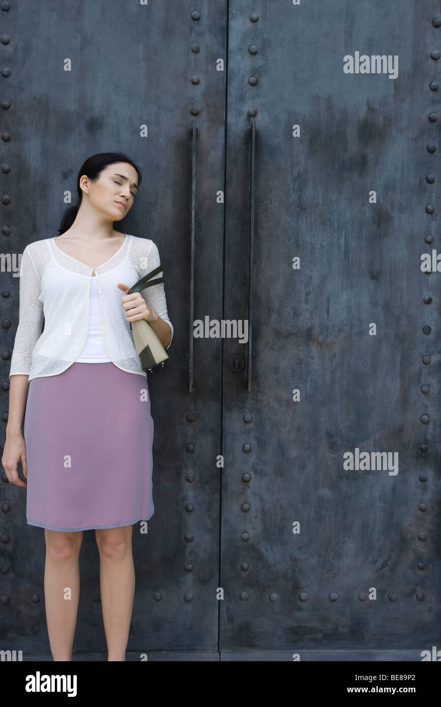 Woman standing beside double doors, eyes closed, frowning Stock Photo ...