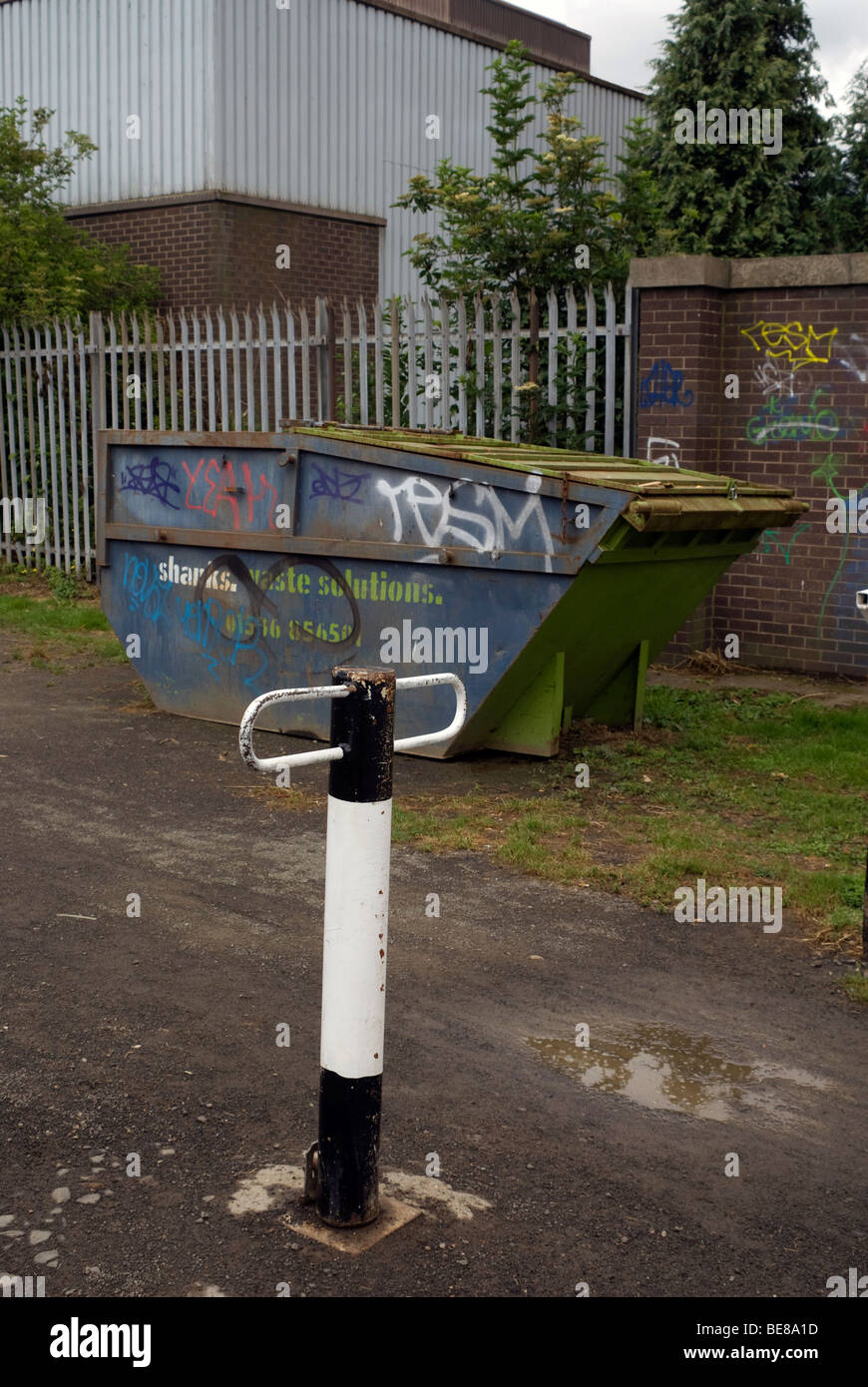 A skip on waste ground, with a black and white post in the foreground ...