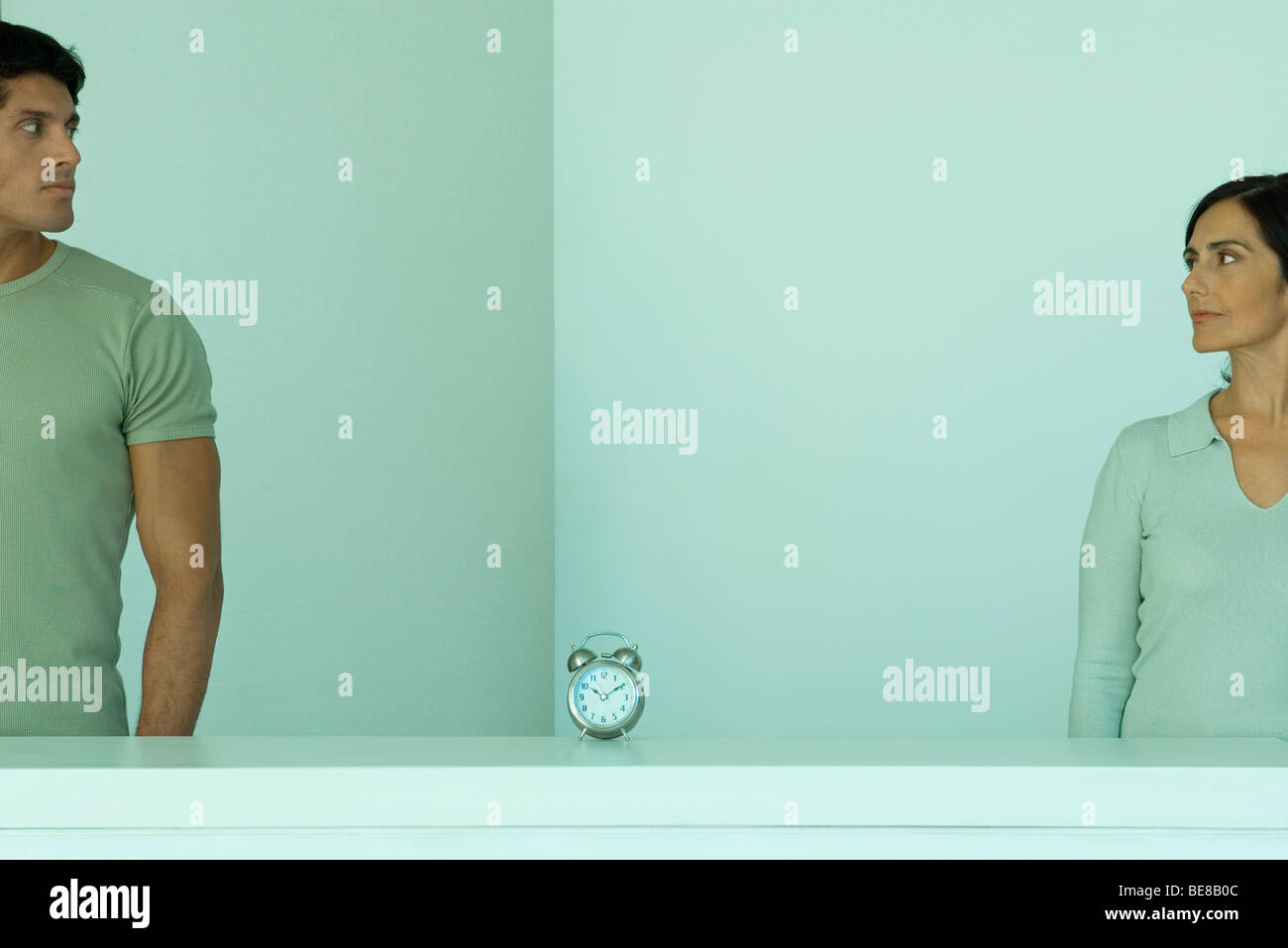 Alarm clock set on counter between man and woman looking at each other ...