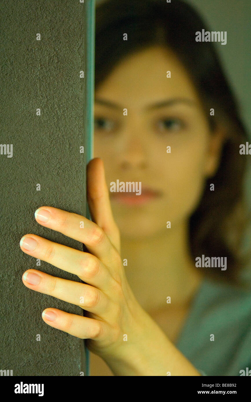 Young woman holding on to wall, looking around corner Stock Photo - Alamy