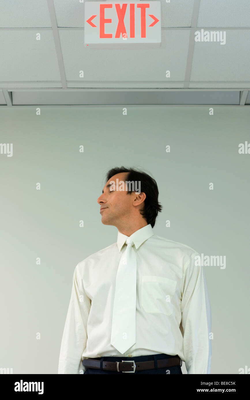 Man standing beneath exit sign with eyes closed Stock Photo - Alamy