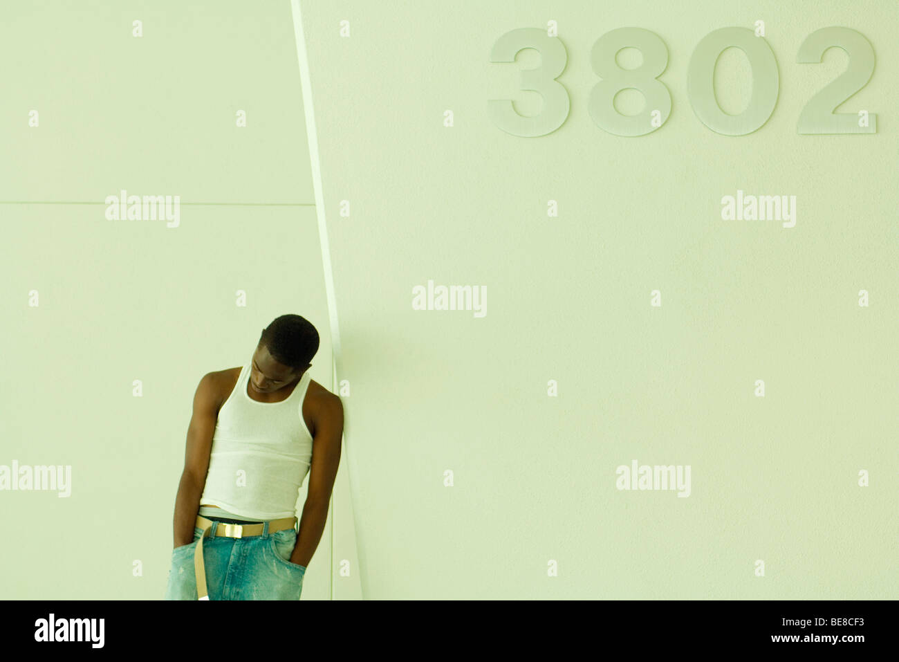 Young male leaning against wall with hands in pockets, head down Stock ...