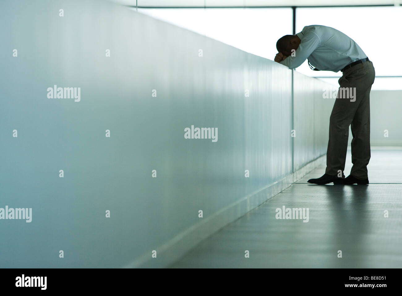 Man standing in corridor, bending over with head resting on arms, side ...