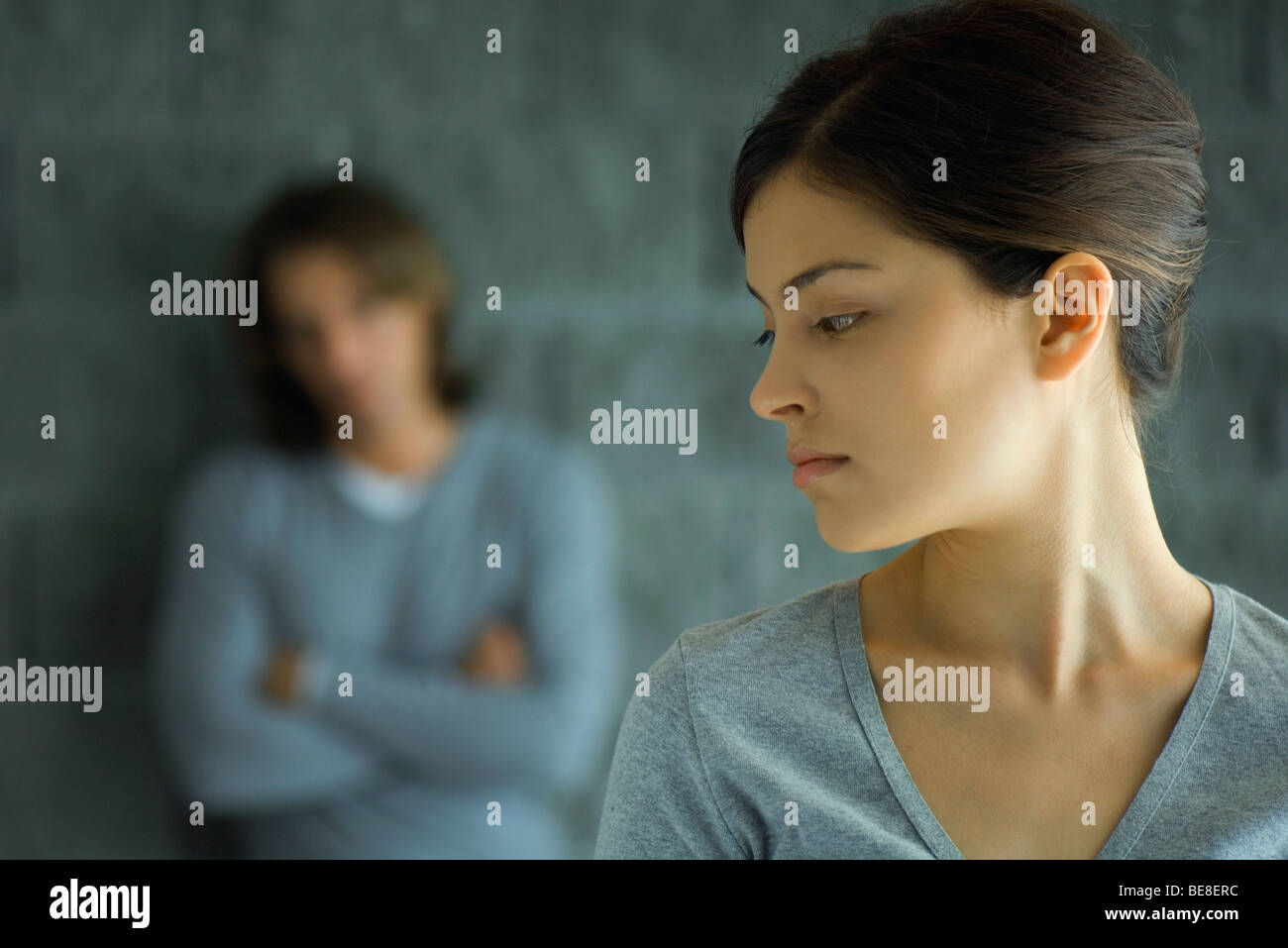 Young woman looking over shoulder, man in background leaning against ...