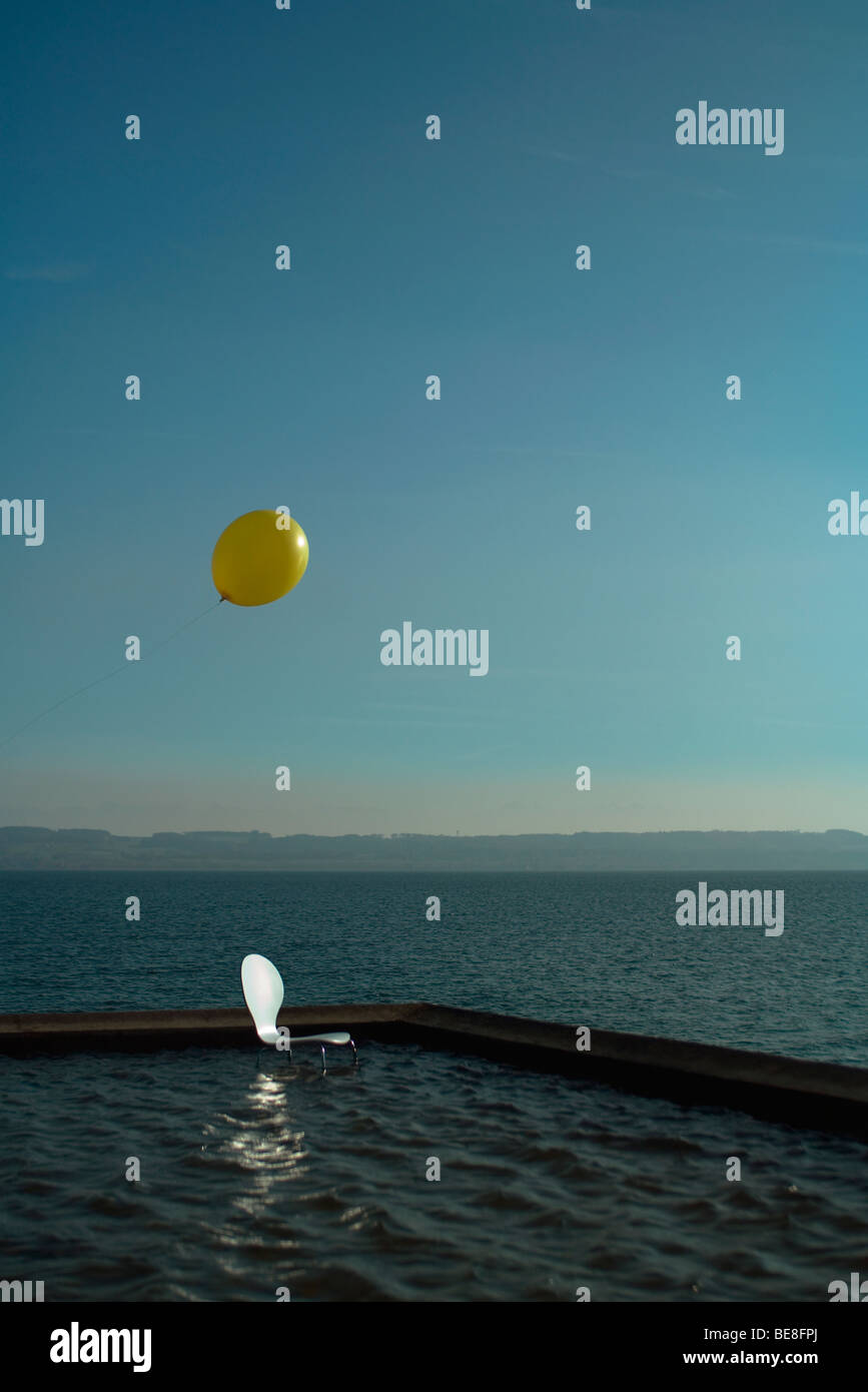 Chair placed in lake near breakwater, balloon floating overhead Stock ...