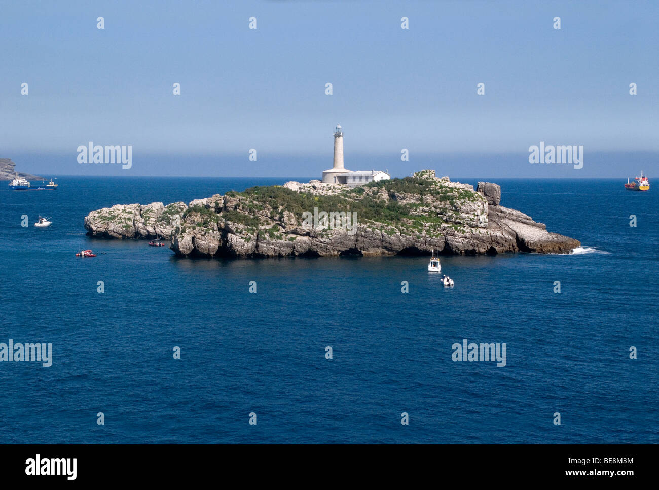 Pretty small rock island with a white lighthouse in clear blue sea and ...
