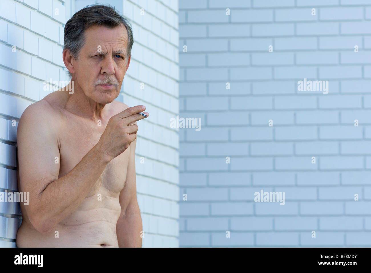 Bare-chested man leaning against wall smoking Stock Photo - Alamy