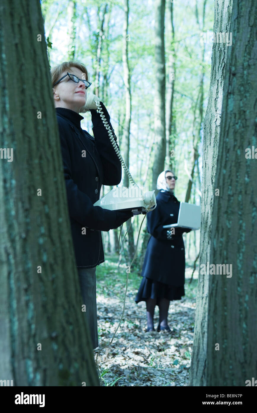 Two women standing in woods, one using landline phone, the other ...