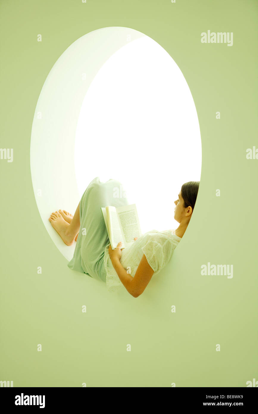 Young woman reclining on windowsill, reading book Stock Photo - Alamy