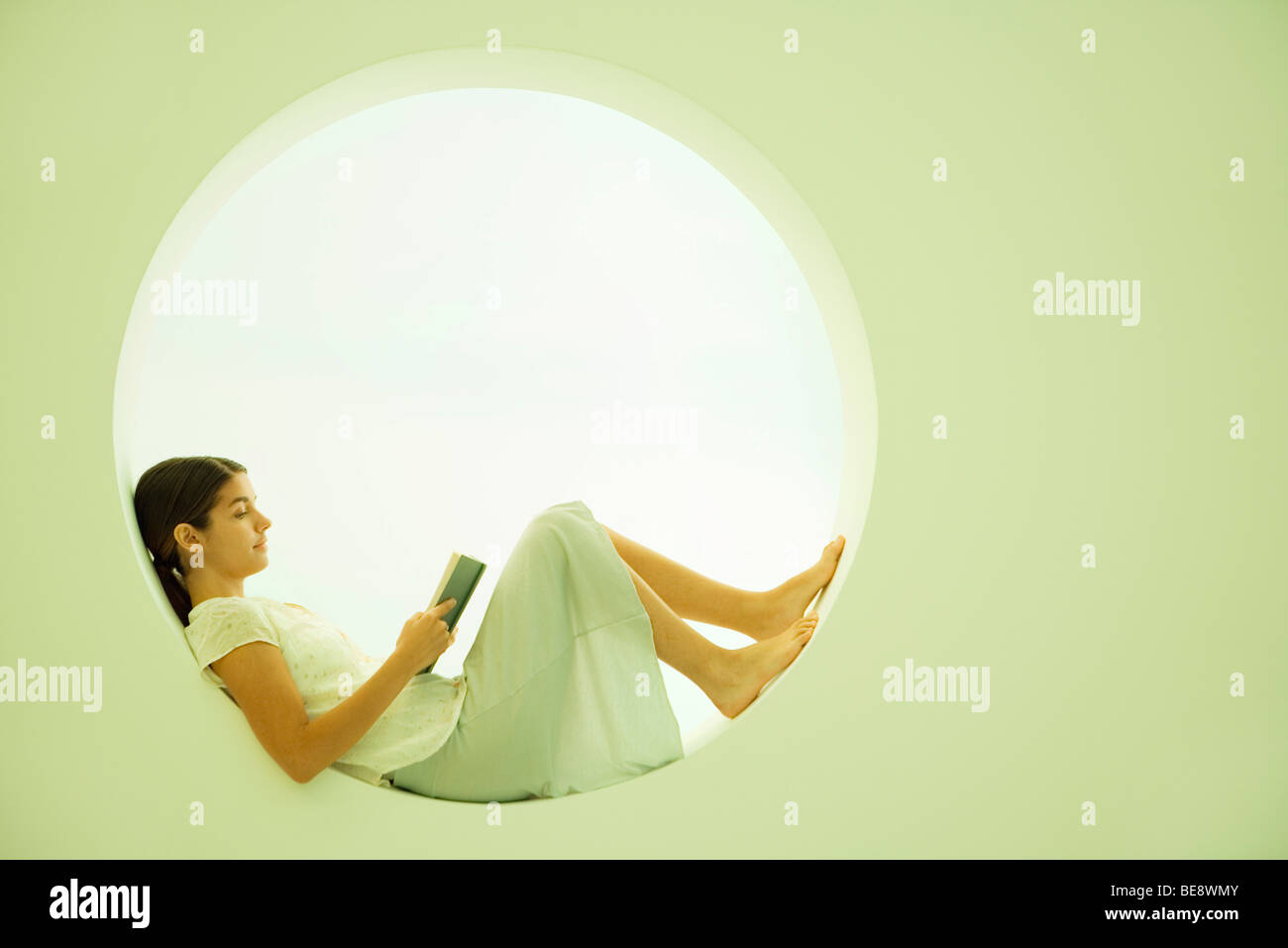 Young woman reclining on windowsill, reading book Stock Photo - Alamy