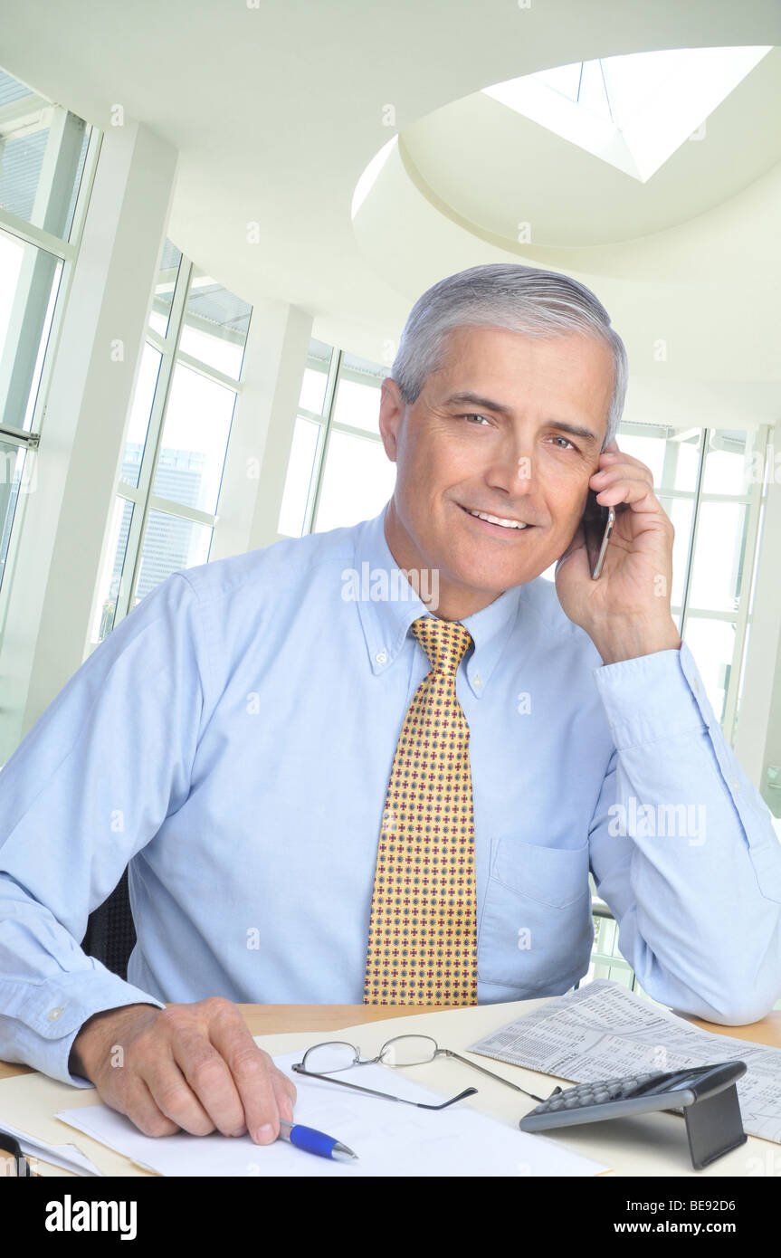 Businessman Sitting at Desk Talking on Cell Phone in office setting ...