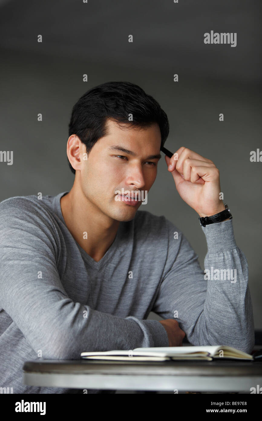 Asian man sitting at table and thinking Stock Photo - Alamy