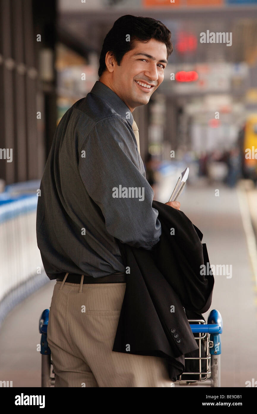 Man pushing trolley in airport, smiling at camera Stock Photo - Alamy