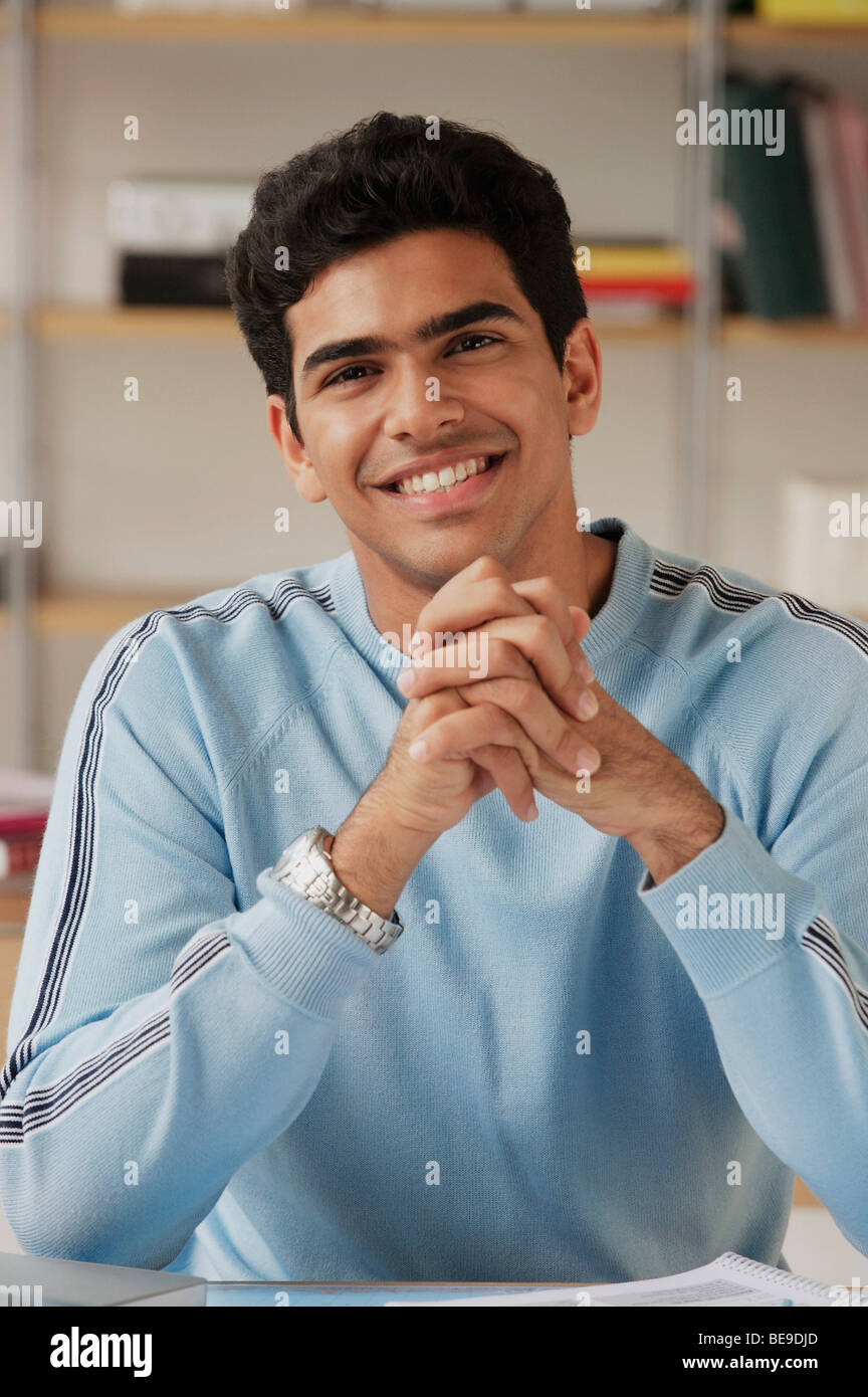 Young man sitting at desk and smiling at camera Stock Photo - Alamy