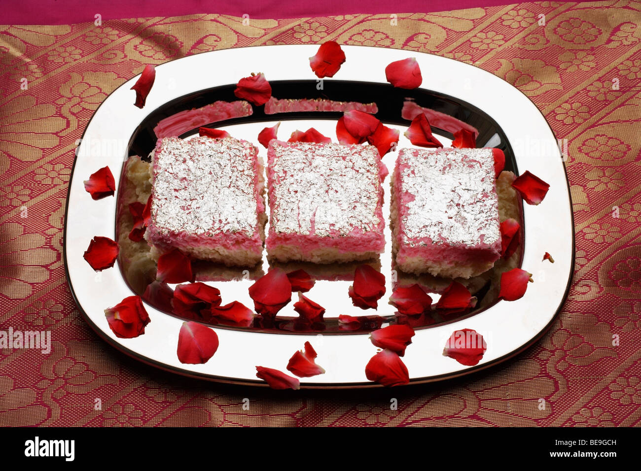 Indian pink sweets on silver tray with rose petals Stock Photo - Alamy