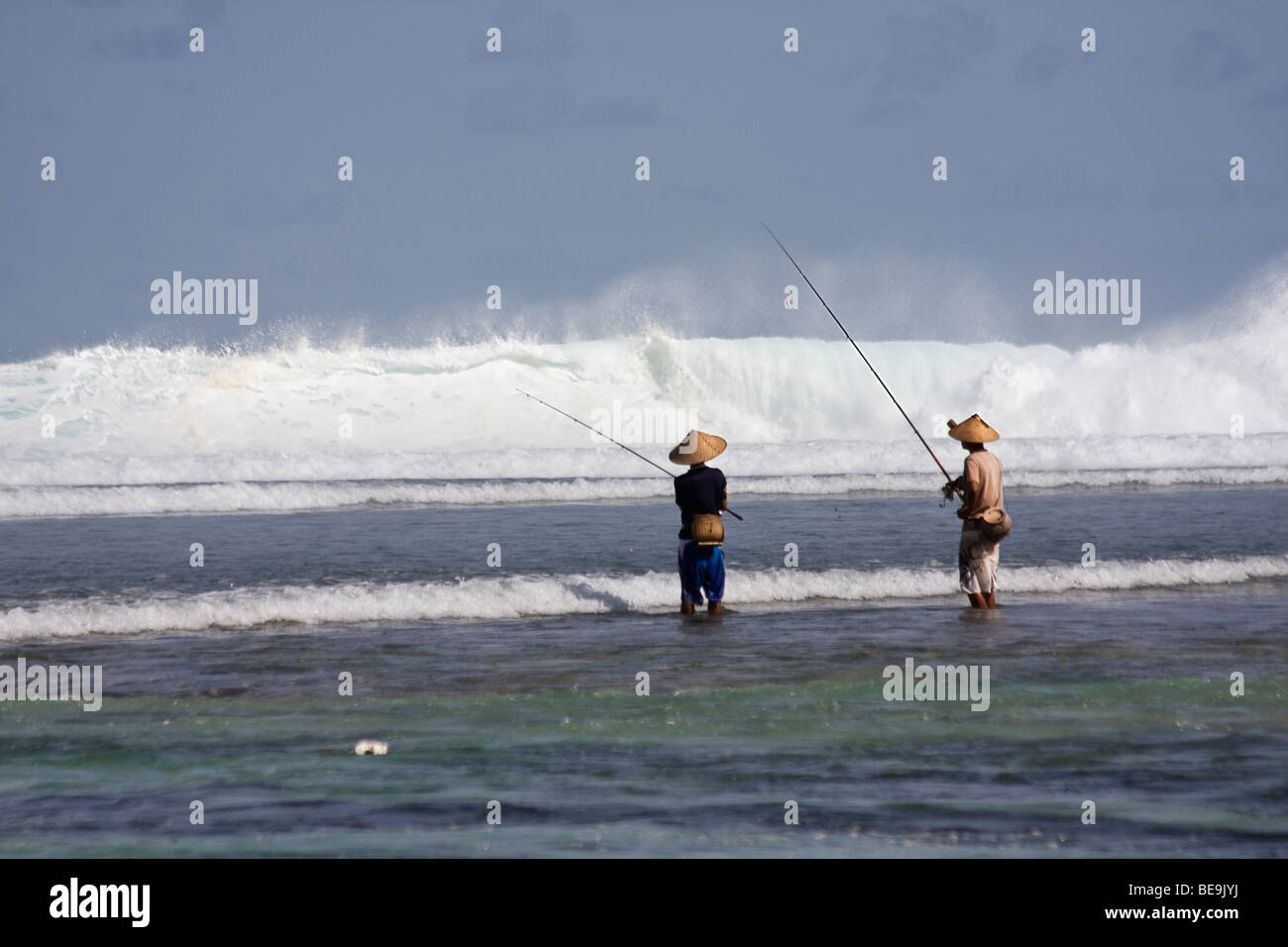 Two fishermen with conical hat fishing sheltered by the coral reef with ...