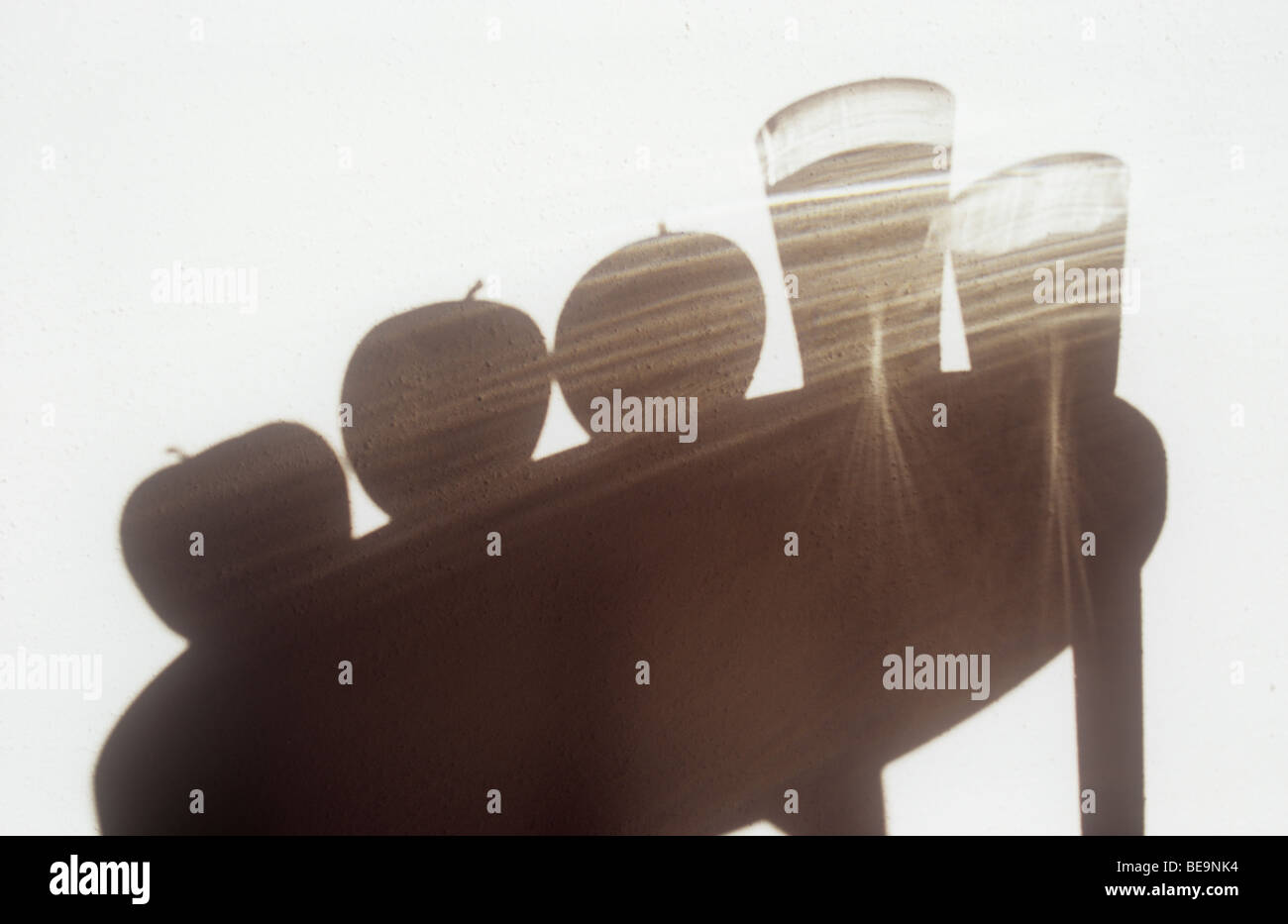 Shadow on white textured wall of circular table with three apples and ...