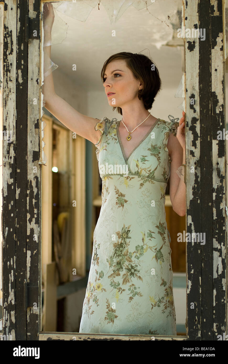 A young woman wearing a dress looks out from the broken window of a ...