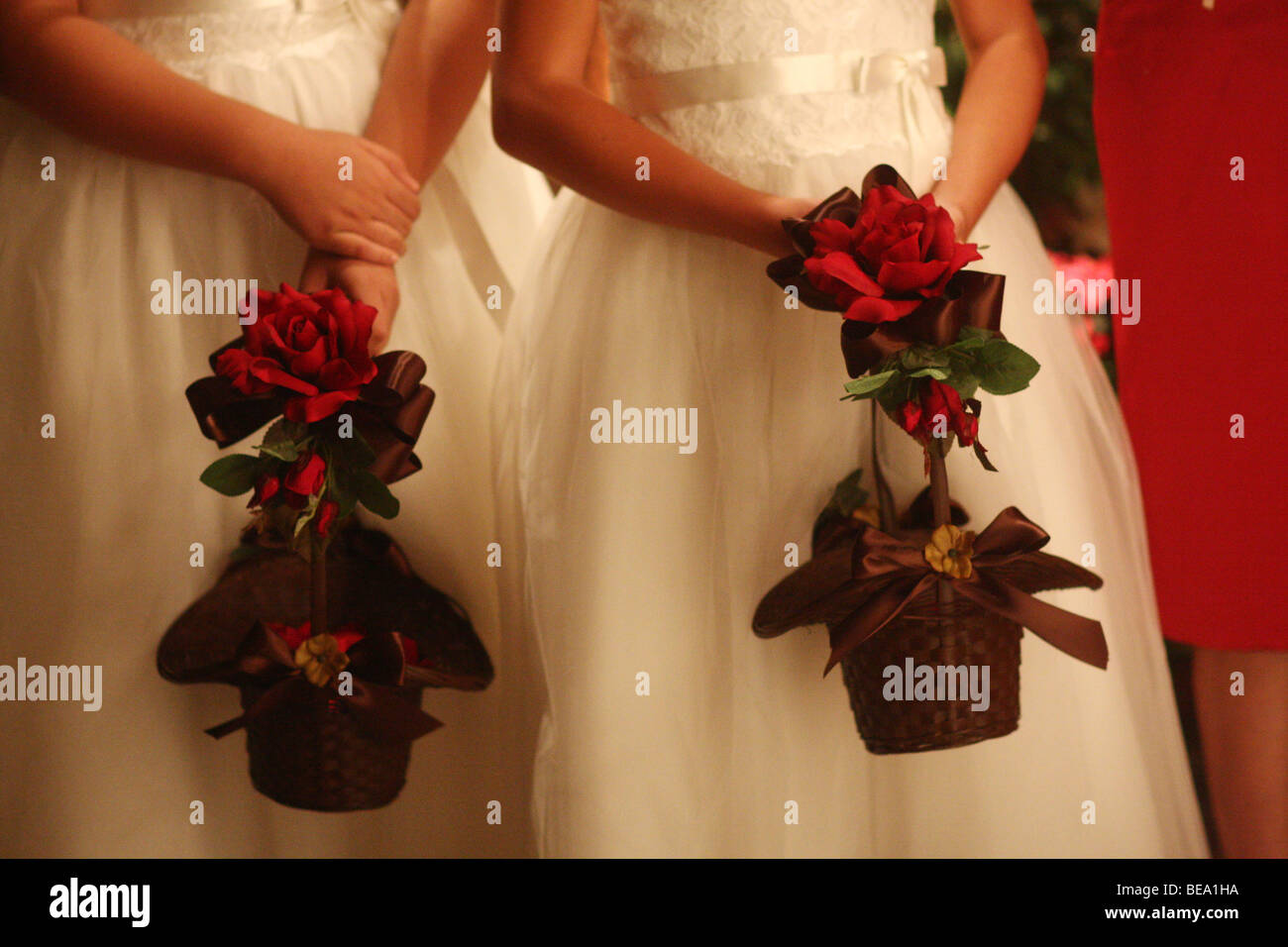 Two flower girls at a wedding hold baskets decorated with roses. Orange ...