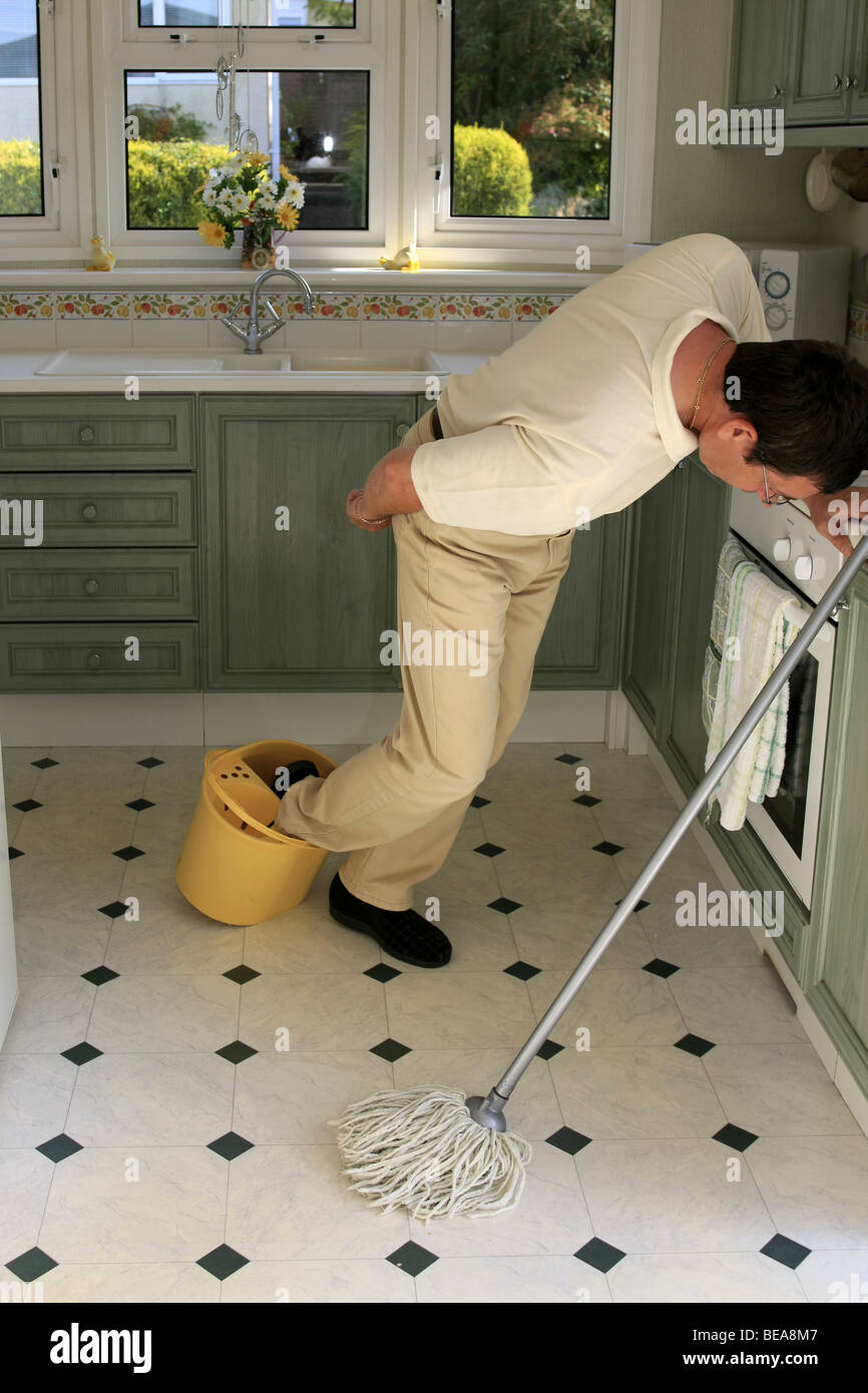 A man using a mop and bucket to clean a kitchen floor tripping over the ...