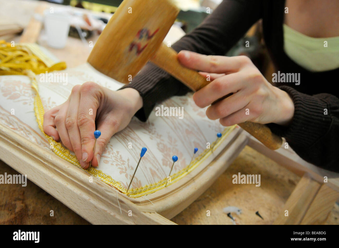 Young woman, upholsterer, fixing a braid on the backrest of an armchair ...