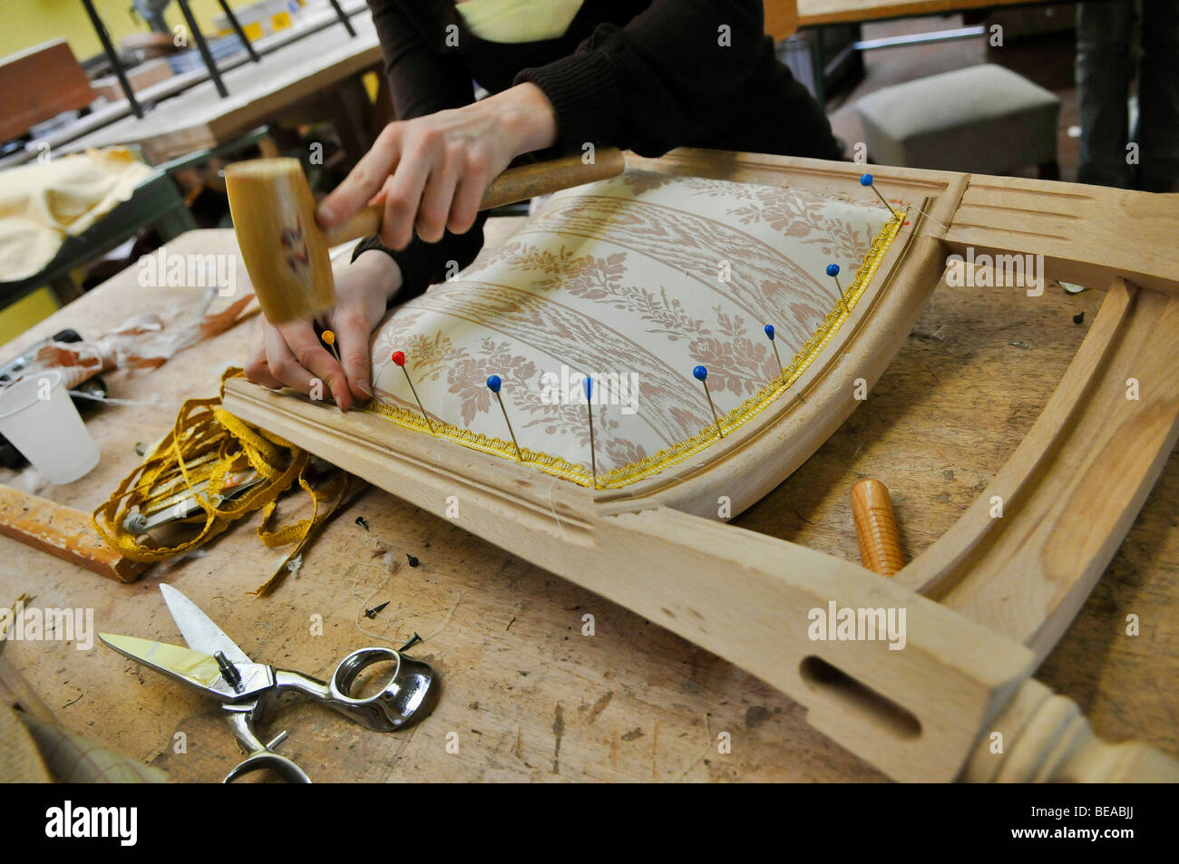 Young woman, upholsterer, fixing a braid on the backrest of an armchair ...