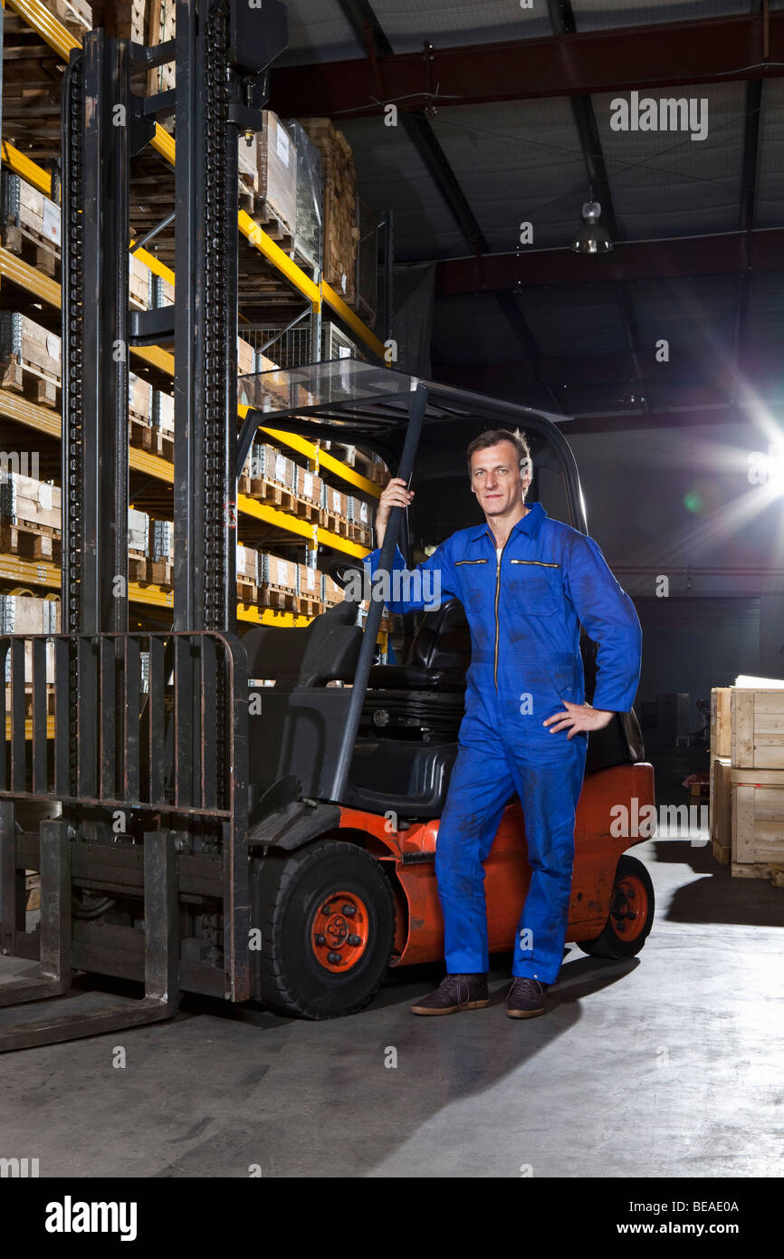 A manual worker standing next to a forklift in a metal parts warehouse ...