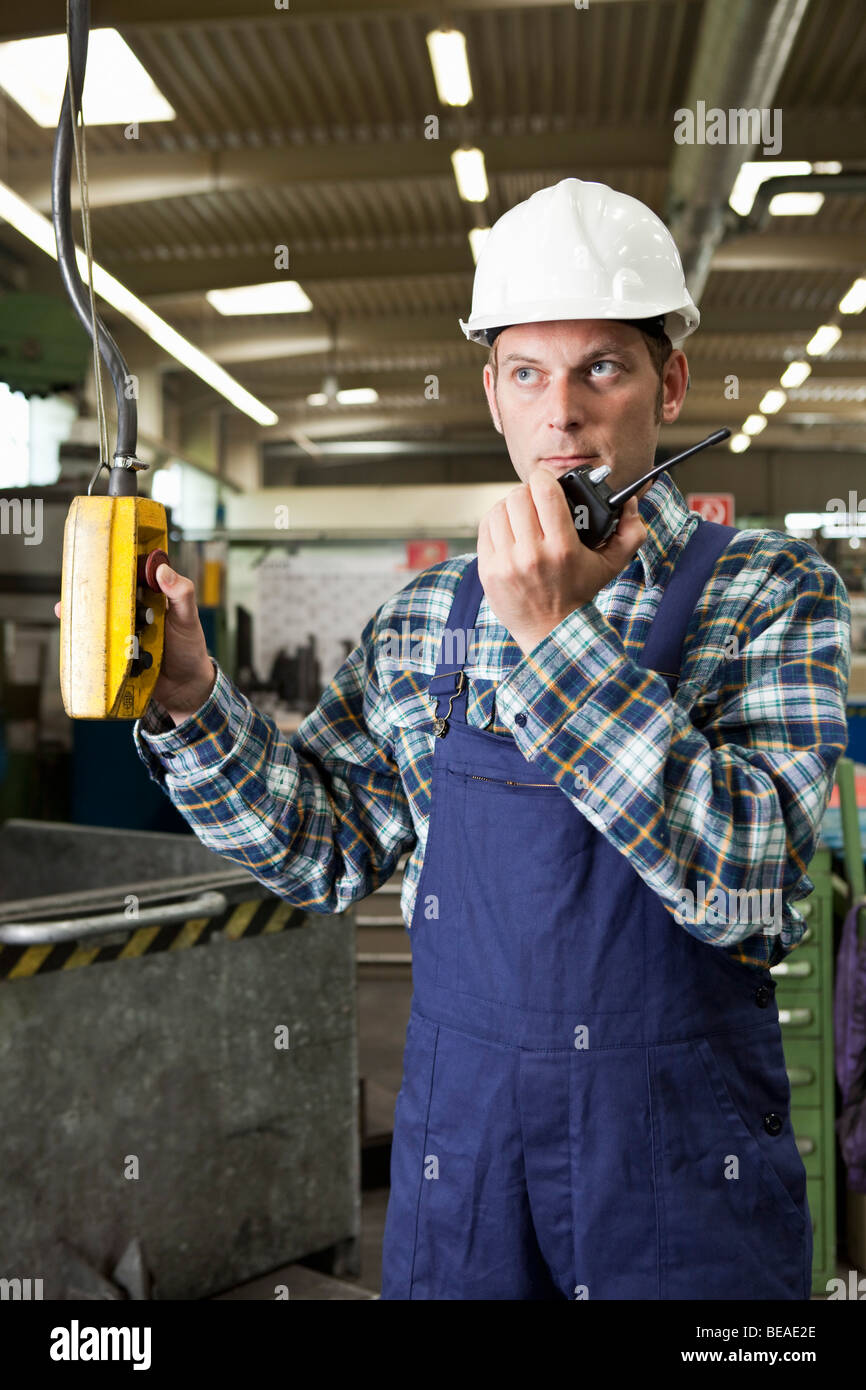 A factory worker using a walkie-talkie and operating a factory machine ...