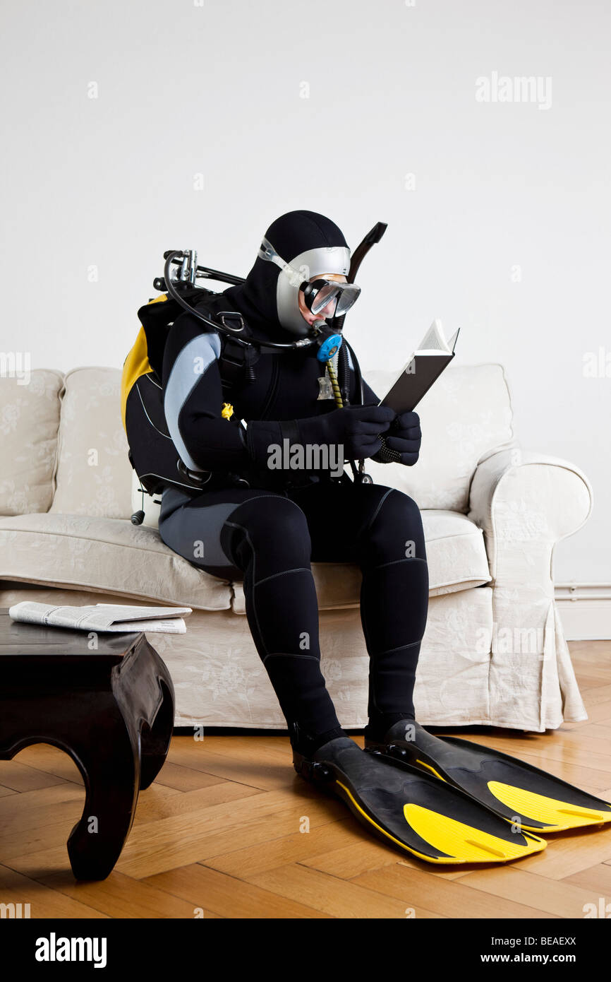 A scuba diver sitting on a couch reading a book Stock Photo - Alamy