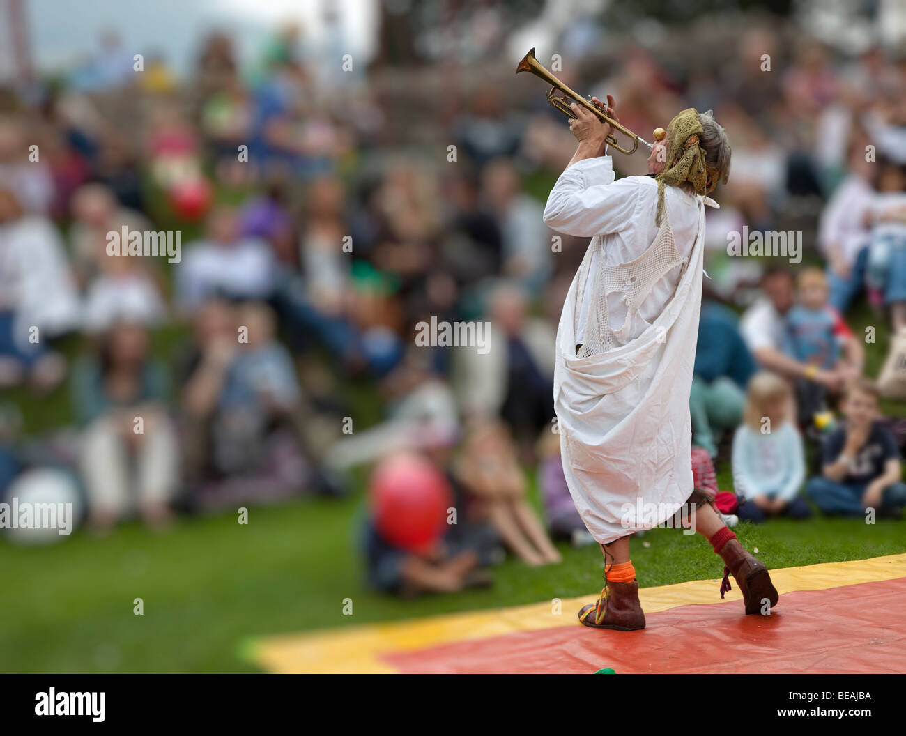 Clown playing a trumpet to an audience outdoors at Abergavenny Food ...