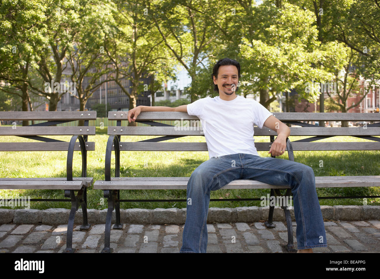 Mixed race man smiling on park bench Stock Photo - Alamy