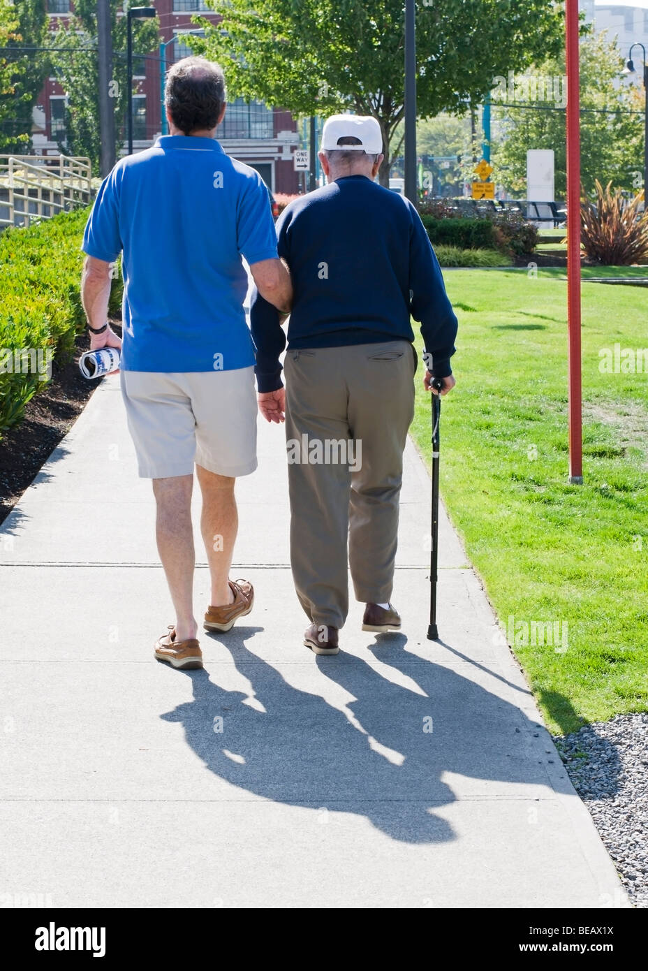 Back view of two men walking in an urban area on a sunny afternoon. One ...