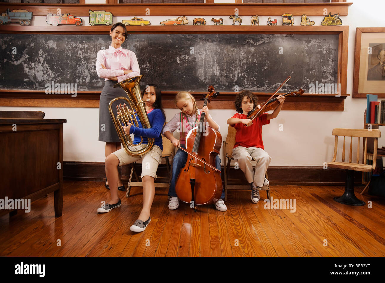 Students playing musical instruments with their teacher standing beside ...