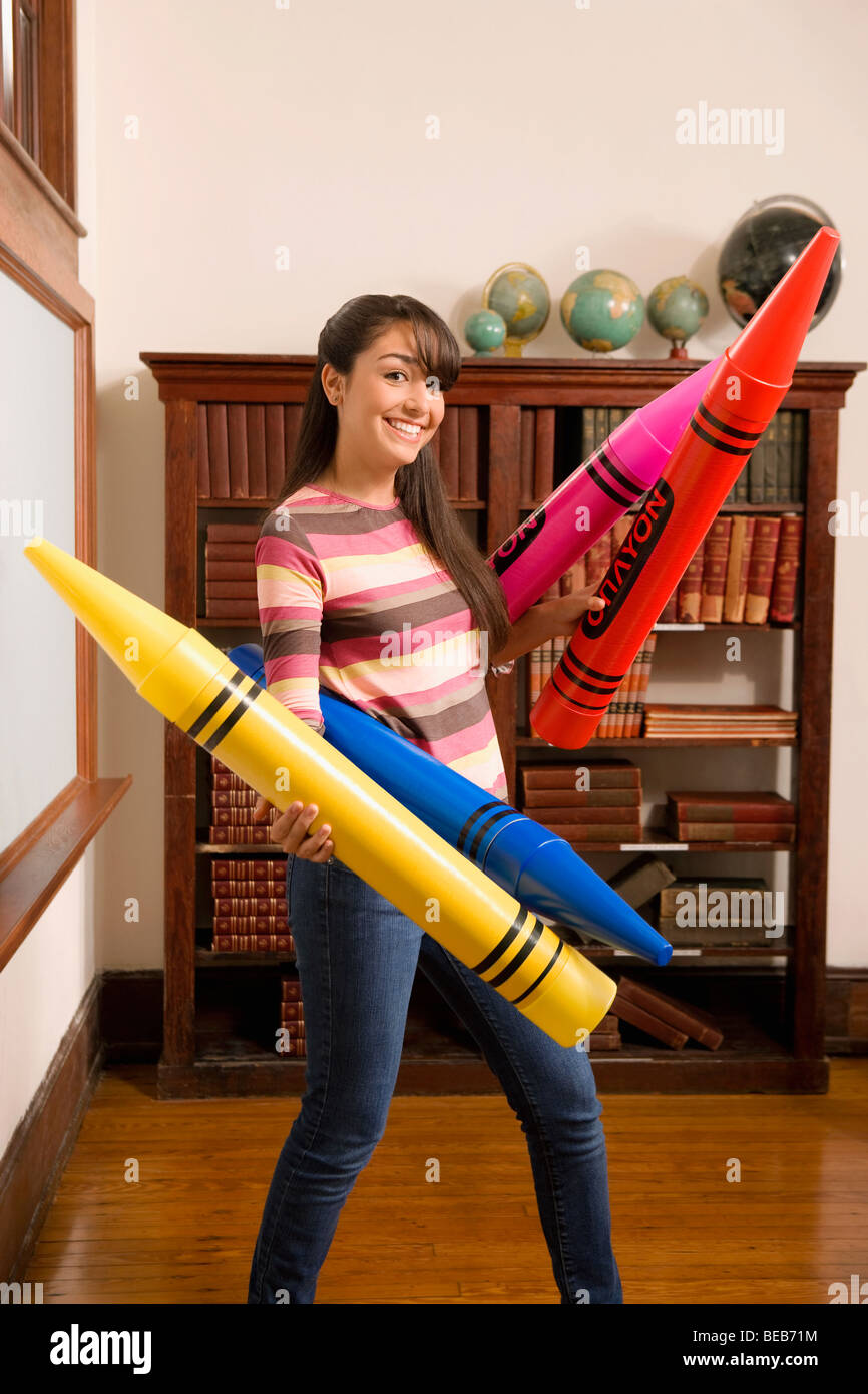 Teenage girl holding oversized crayons and smiling Stock Photo - Alamy