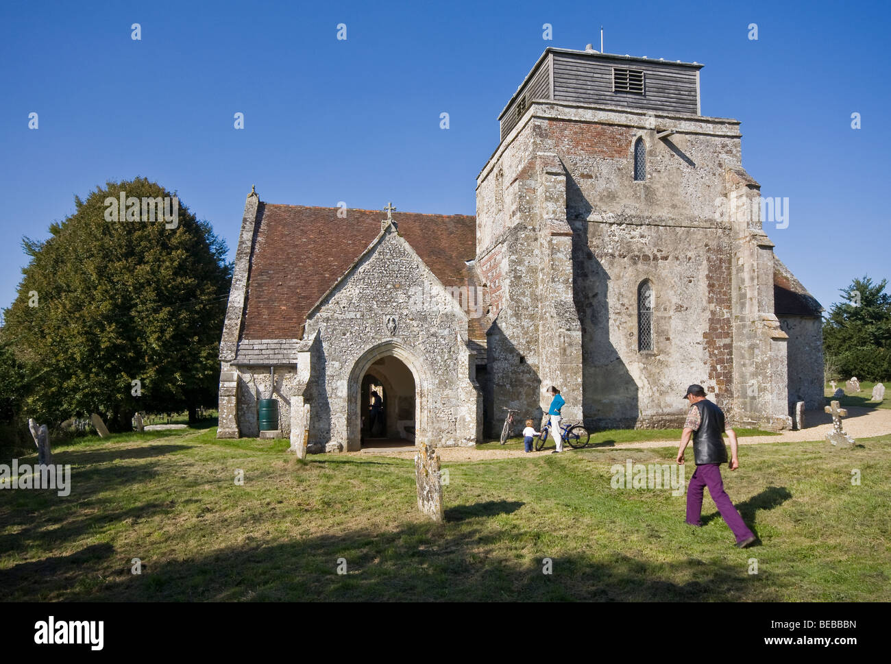 A village church in Summer. A man strides across the graveyard whilst a ...