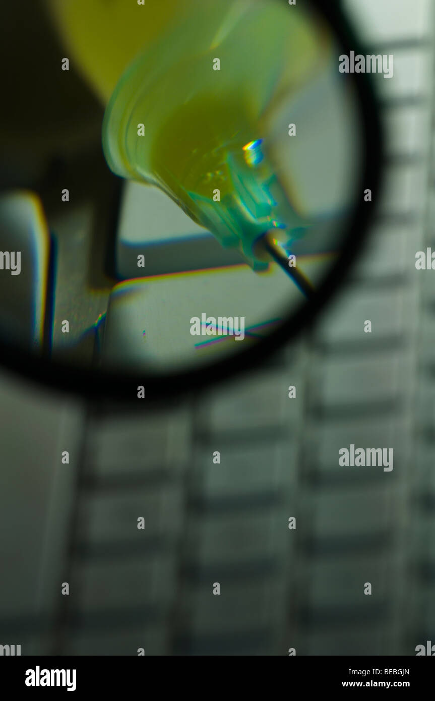 Examining a syringe over a keyboard with a magnifying glass Stock Photo ...