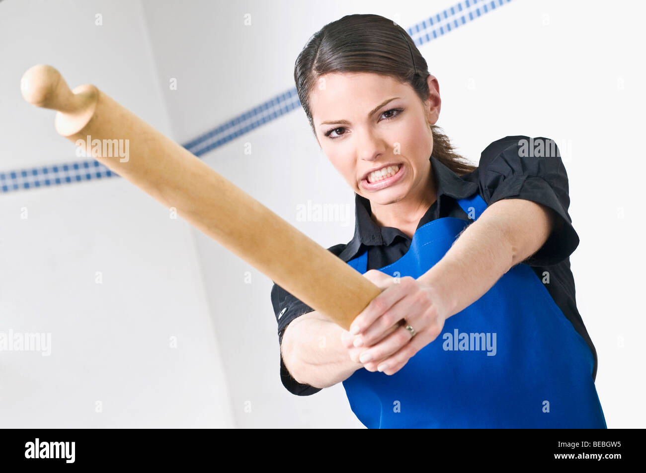 Portrait of a female chef holding a rolling pin and clenching her teeth ...
