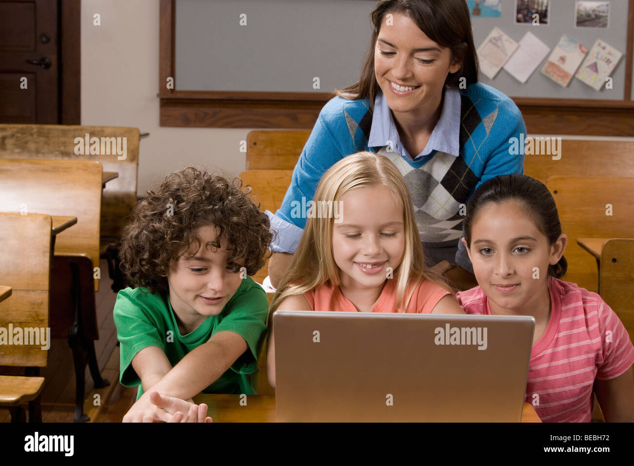 Students working on a laptop in a classroom with their teacher behind them Stock Photo - Alamy