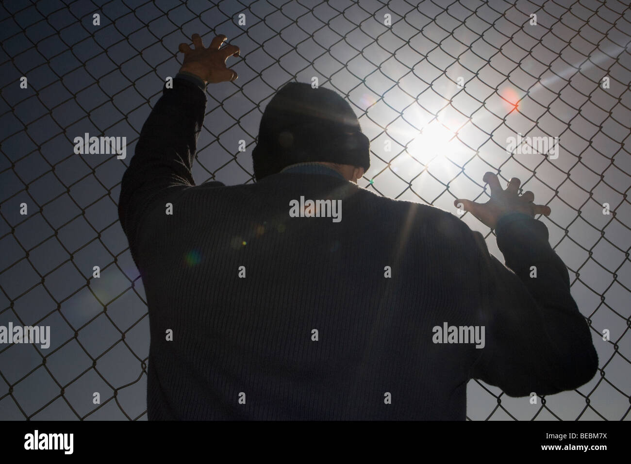 Rear view of a man looking through a chainlink fence Stock Photo - Alamy