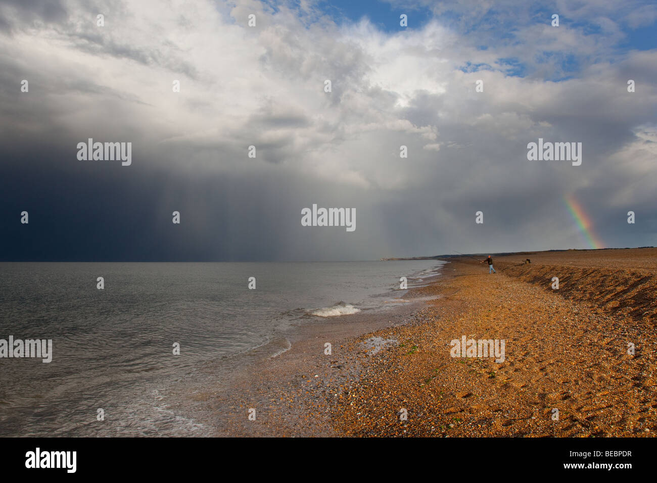 Lone fisherman and rainbow Cley Beach in stormy weather Norfolk UK ...