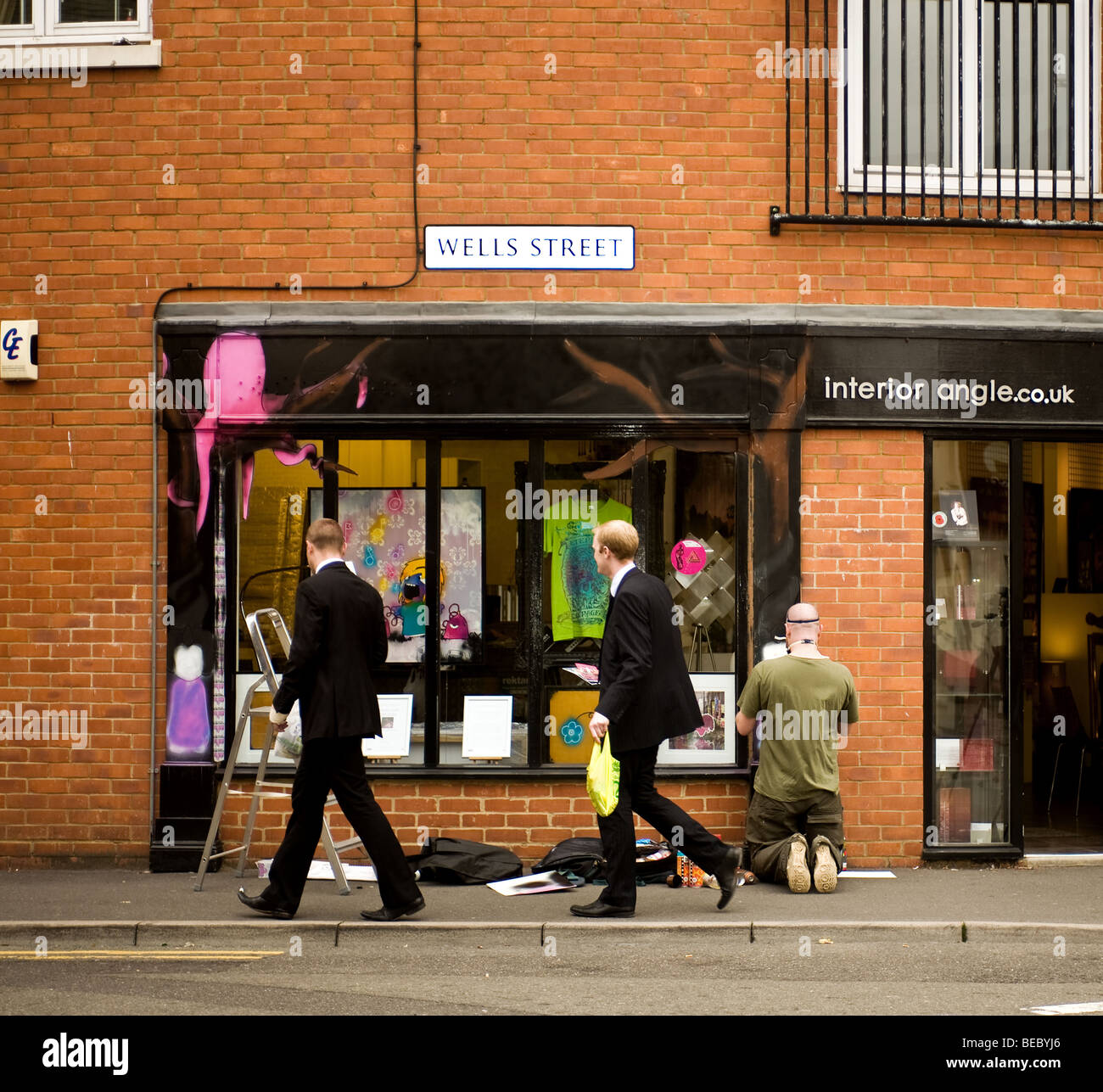 Two men walk past Tom Lewis street artist as he works on a mural on the ...