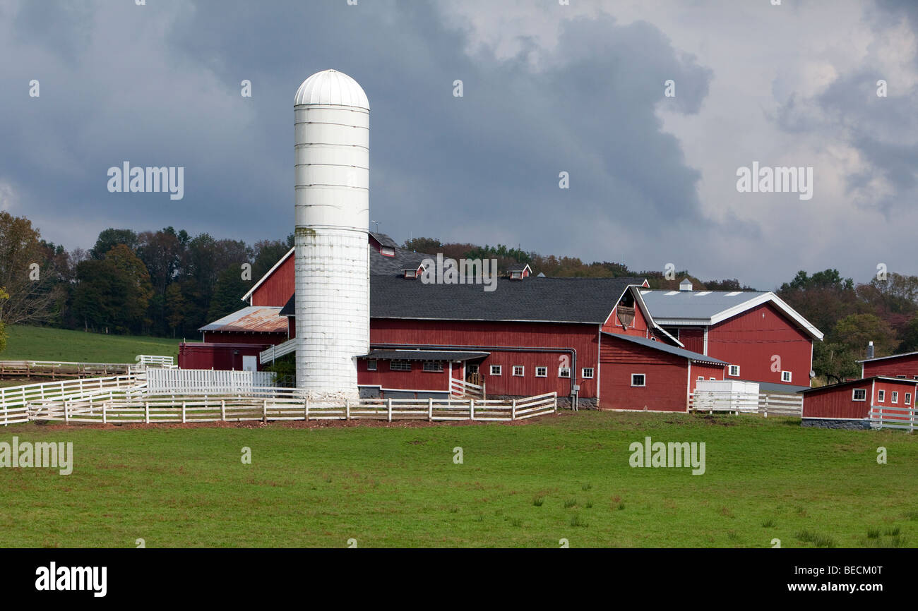 A broad green meadow a red barn with a white silo against a stormy sky ...