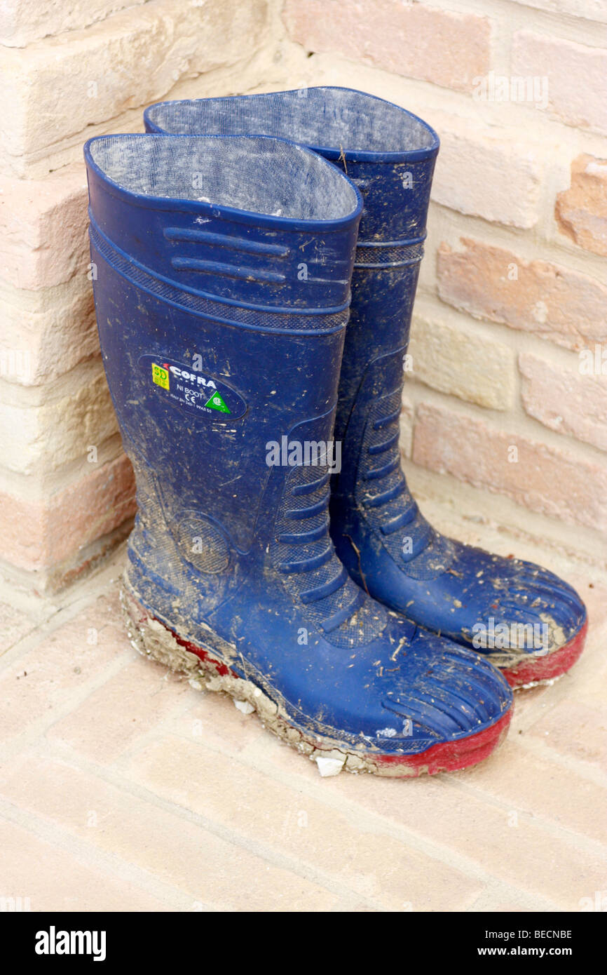mud caked blue wellington boots neatly paced against a brick wall Stock ...