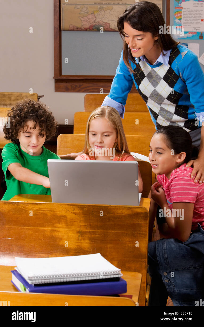 Students with their teacher using a laptop in a classroom Stock Photo ...