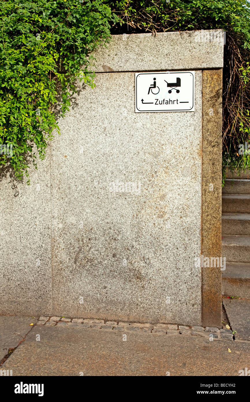 Concrete wall with wheelchair access sign partially covered by green ...