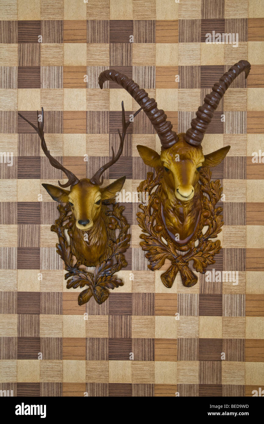 Plastic heads of an ibex and a deer mounted on imitation wood wallpaper ...