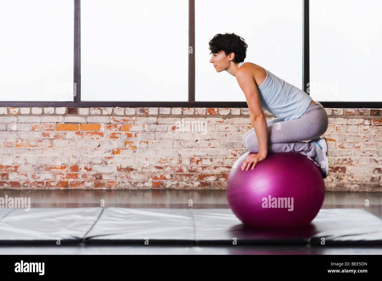 A young woman balancing atop an exercise ball while kneeling on it ...