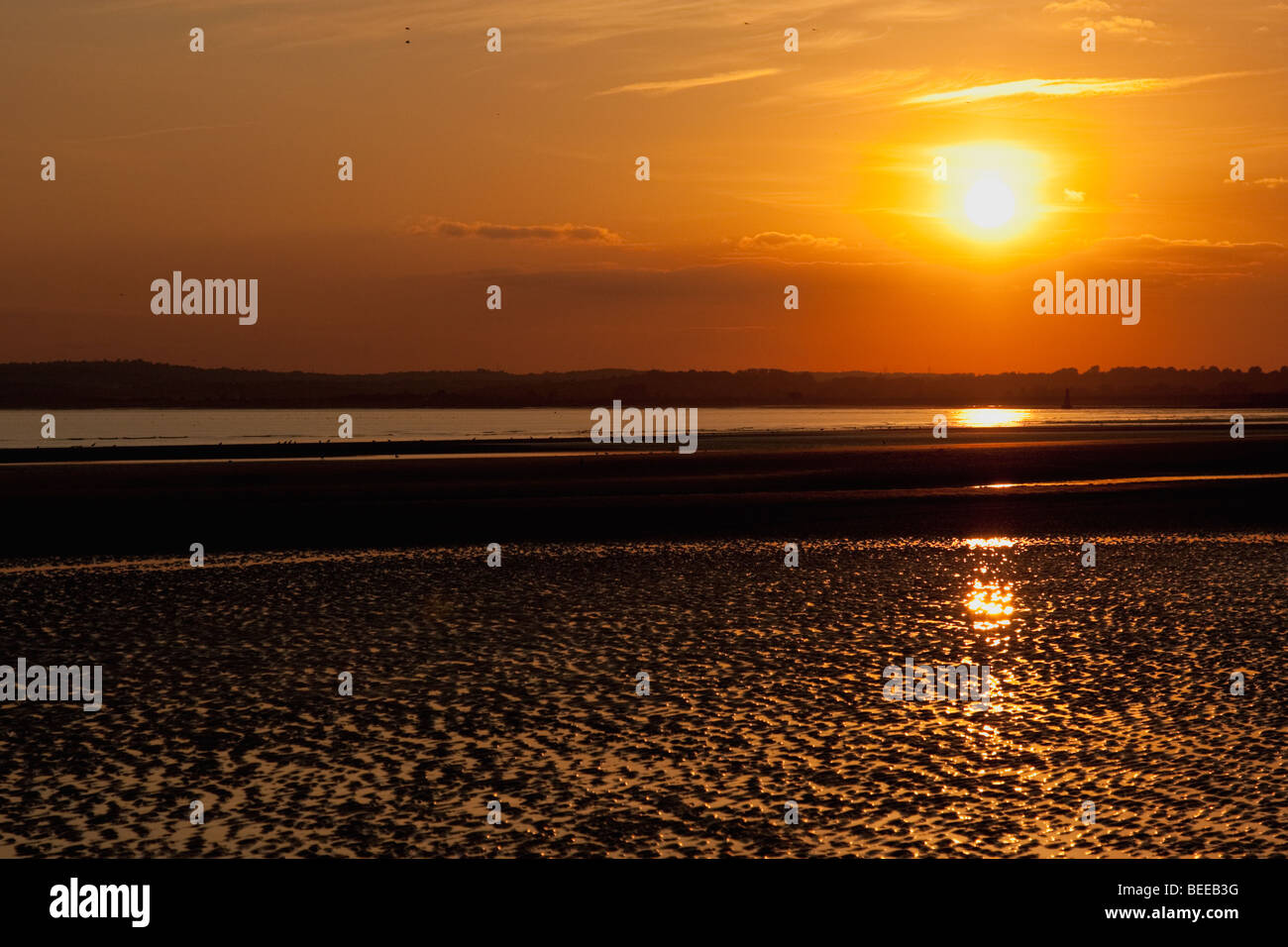 A large bright sun sets over Camber Sands in England UK. Deep orange ...